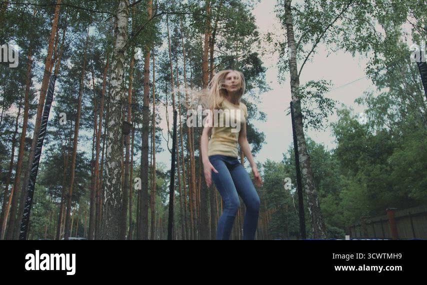 Happy female jumping on trampoline. Beautiful young blond barefoot ...