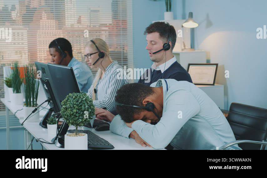 Mixed-race customer support operator falling asleep on his table in ...