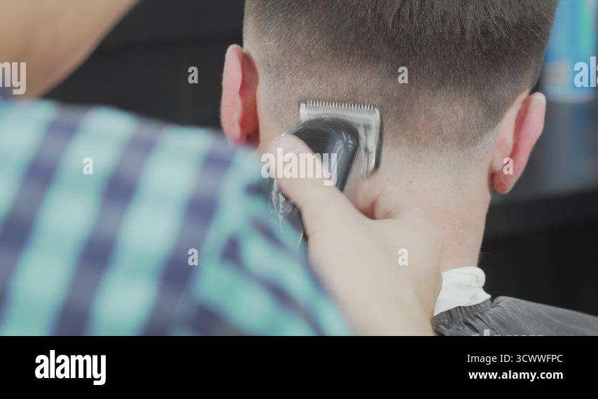 Sliding rear view shot of a barber using a clipper giving a haircut to ...