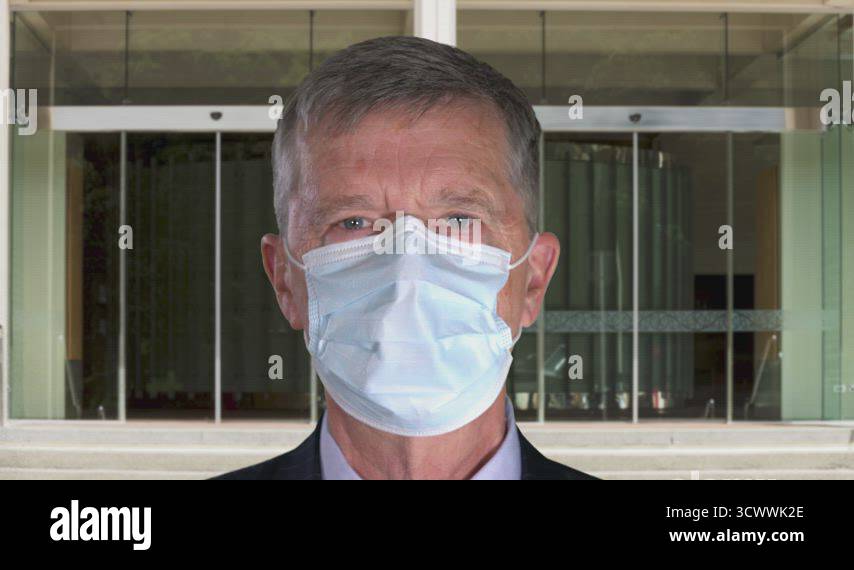 Senior man wearing face mask taking his temperature to check for virus ...