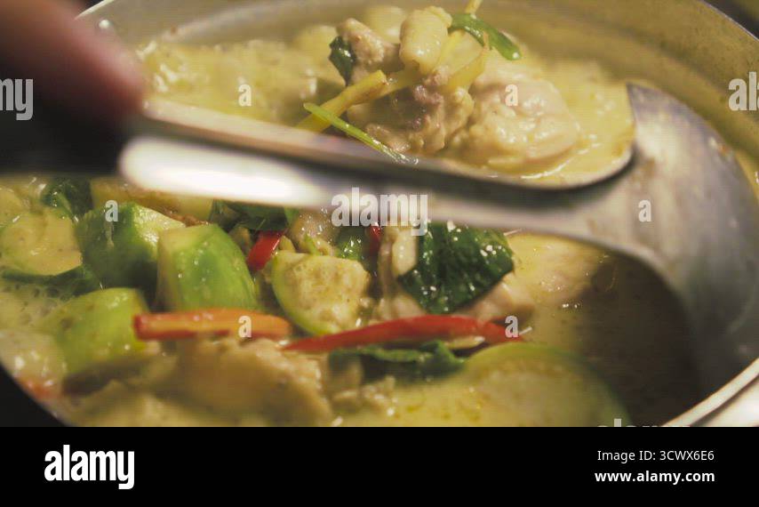 Old lady using ladle for stirring up a curry. Making of Green curry ...