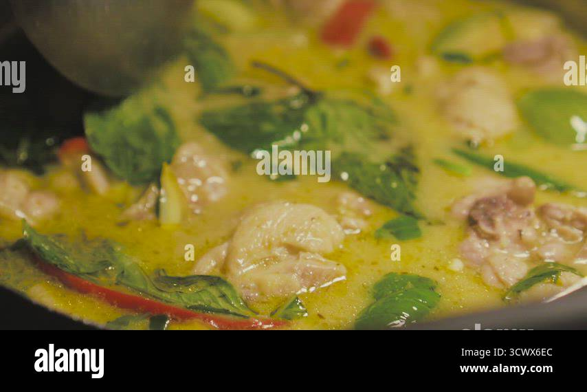 Old lady using ladle for stirring up a curry. Making of Green curry ...