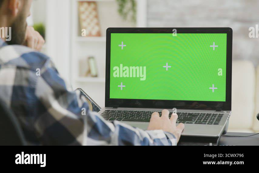 Over the shoulder shot of man working on laptop with green screen ...