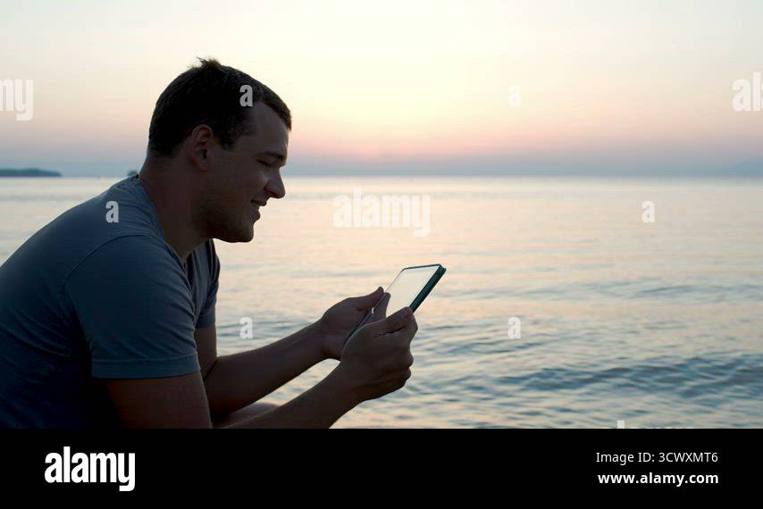 Young man by the sea typing message on pad Stock Video Footage - Alamy
