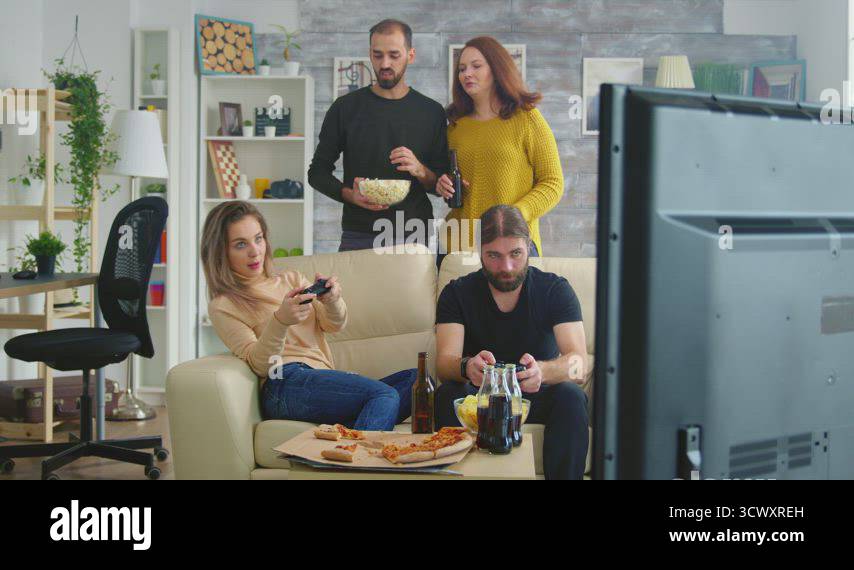 Young couple eating popcorn while their friends are playing video games ...
