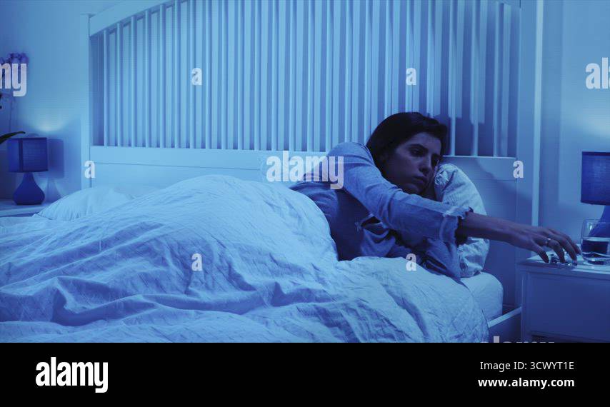 Wide shot of woman at night in bed feeling sick taking pill coronavirus ...