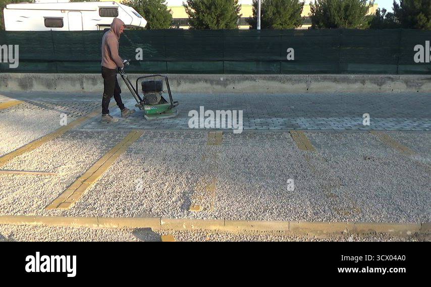 Workers using a vibro-compacting plate to compact self-locking blocks ...