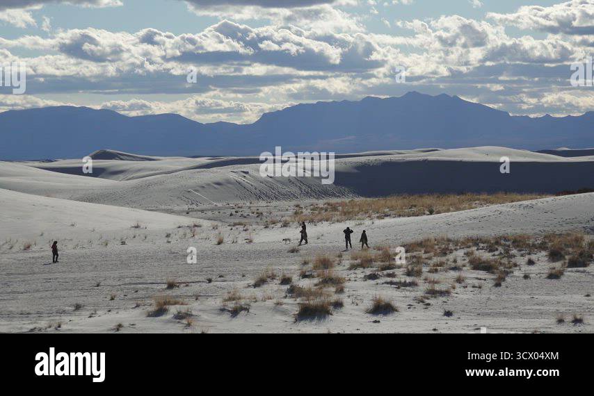 People walk on white gypsum sands in a desert landscape against a ...