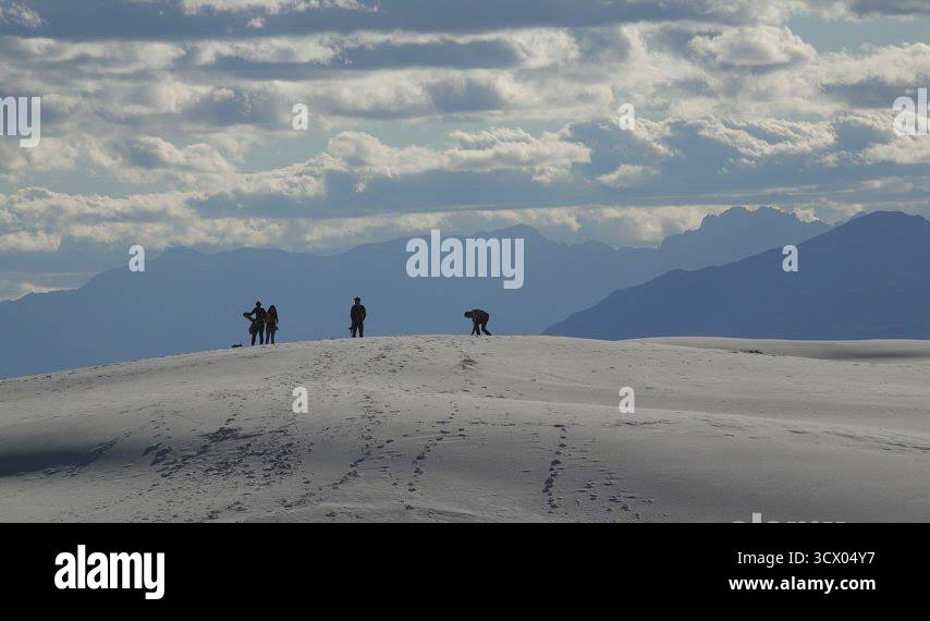 People walk on white gypsum sands in a desert landscape against a ...