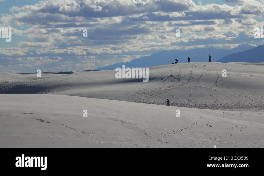 People walk on white gypsum sands in a desert landscape against a ...