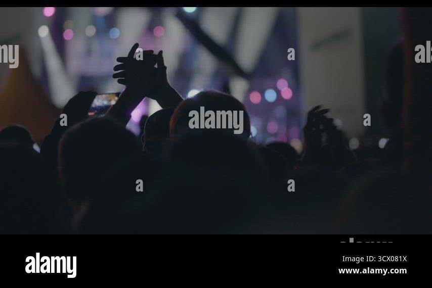 View from behind of hands hold smartphone among people at rave party ...