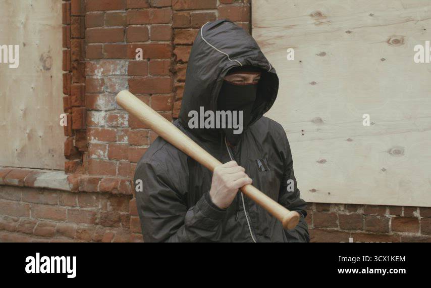 Street bandit in black mask and hood holds baseball bat in criminal ...