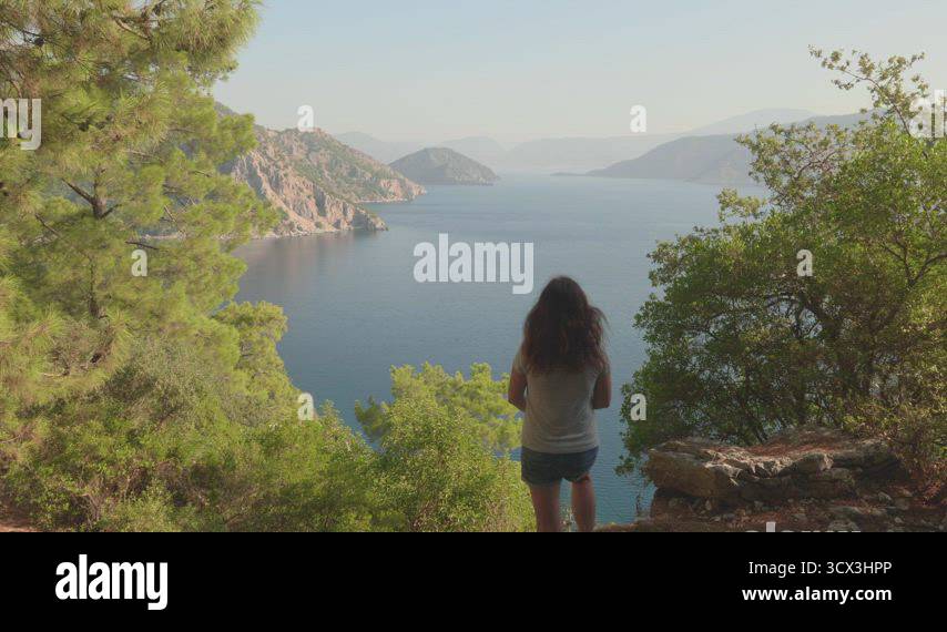 Traveling woman stretching hands on cliff op on mountain lake landscape ...