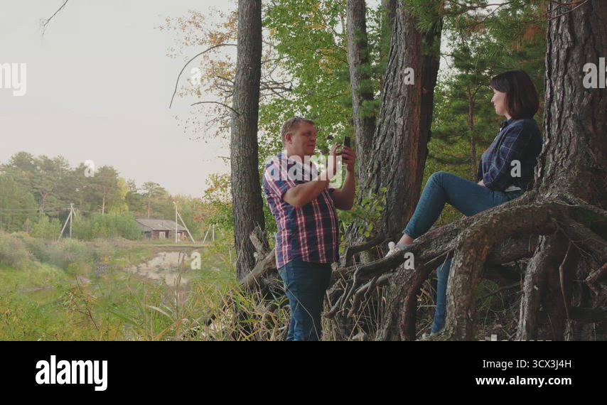 Man photographing woman by mobile phone in coniferous forest. Happy ...