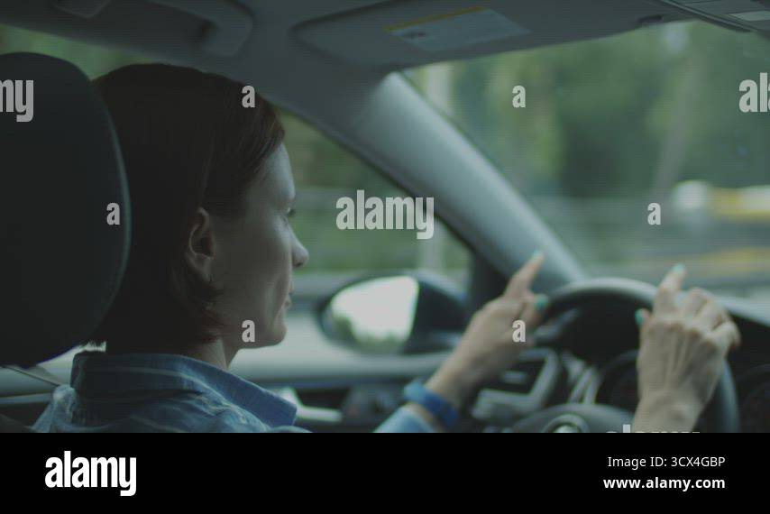 Young 30s woman dancing and singing while driving car in the city. Side ...