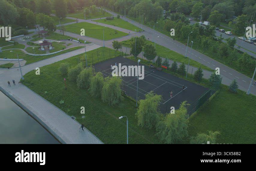 Flying around players playing tennis on a court in green city park ...