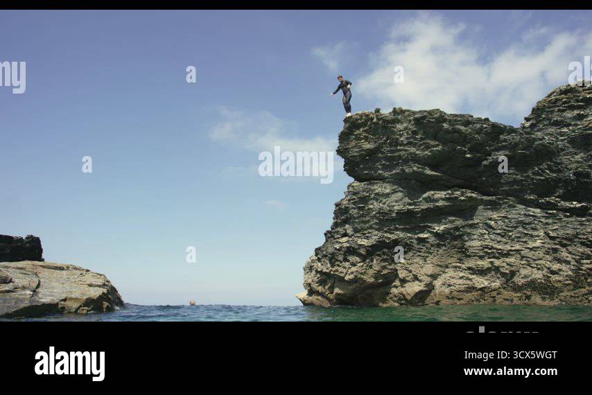 A man wearing a wetsuit diving off a high cliff into the sea Stock ...