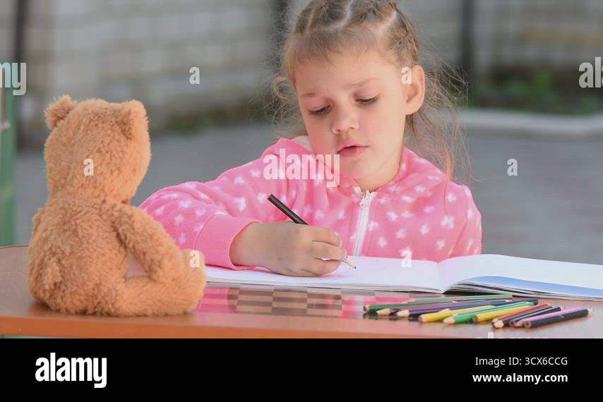 Five-year girl with enthusiasm draws a teddy bear sitting in front of ...