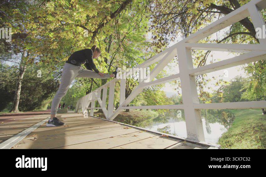 Runner girl stretching her legs on a wooden bridge fence. Warming up ...