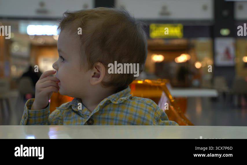 young boy eating french fries at the food court and waving his hand ...