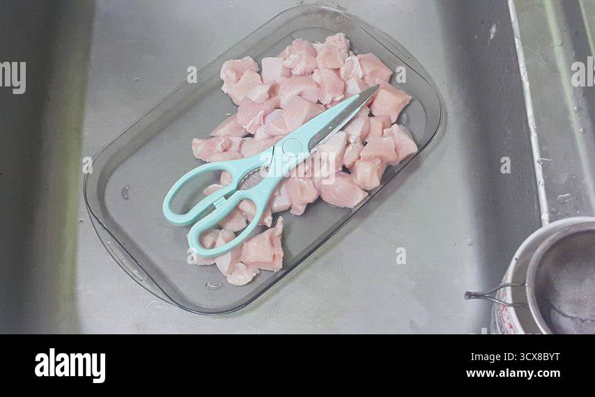 Chicken meat is cut into pieces in kitchen with sharp food scissor ...