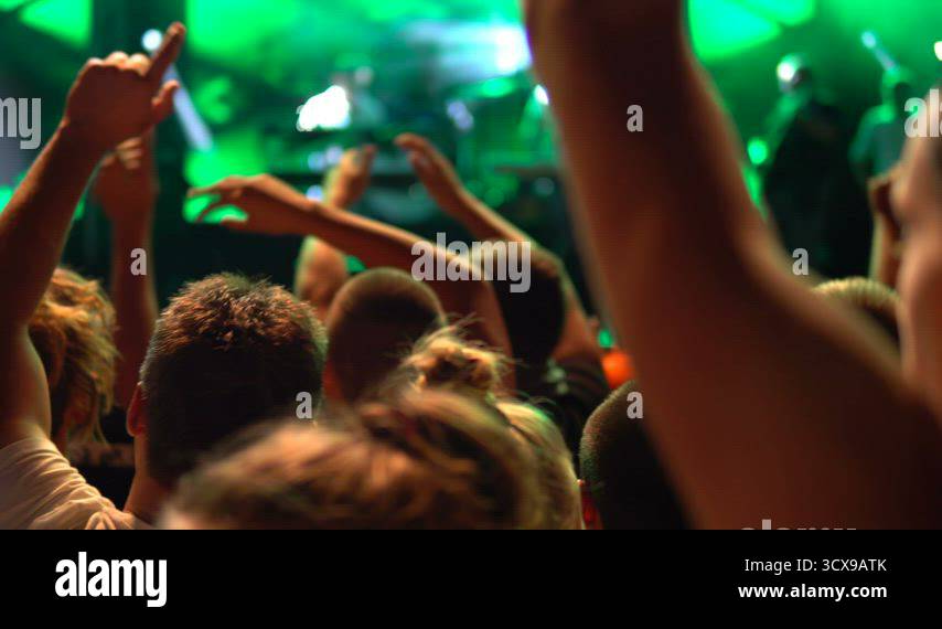 People at a concert silhouetted by the lights with hands rised up ...