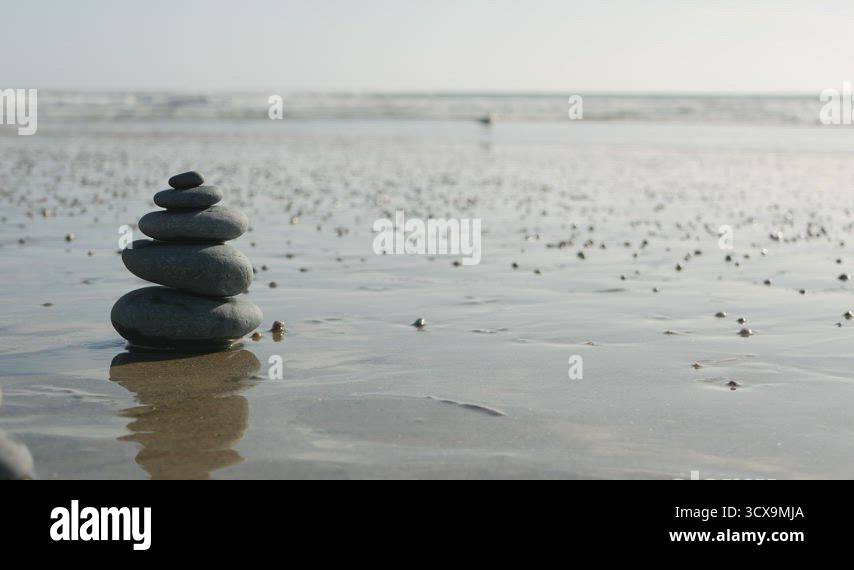 Rock balancing on ocean beach, stones stacking by sea water waves ...