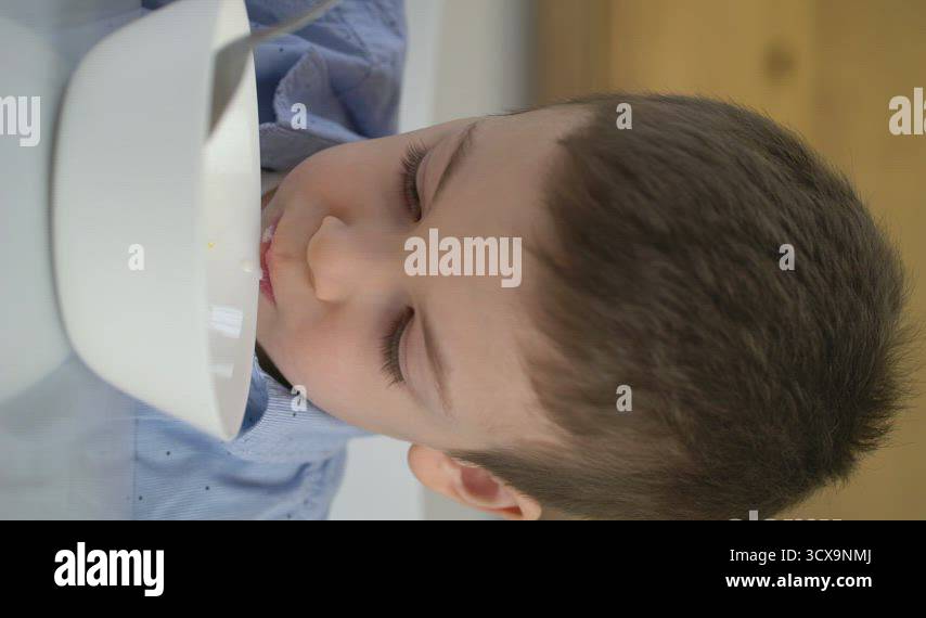 Vertical video. Small hungry boy eating tasting sweet corn flakes with ...