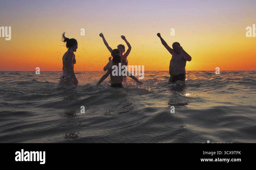 Group of family friends swimming in the sea at sunset into water ...