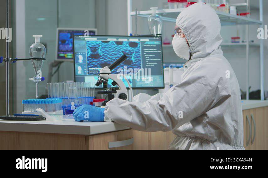 Chemist researcher in coverall looking at bacteria sample from glass ...