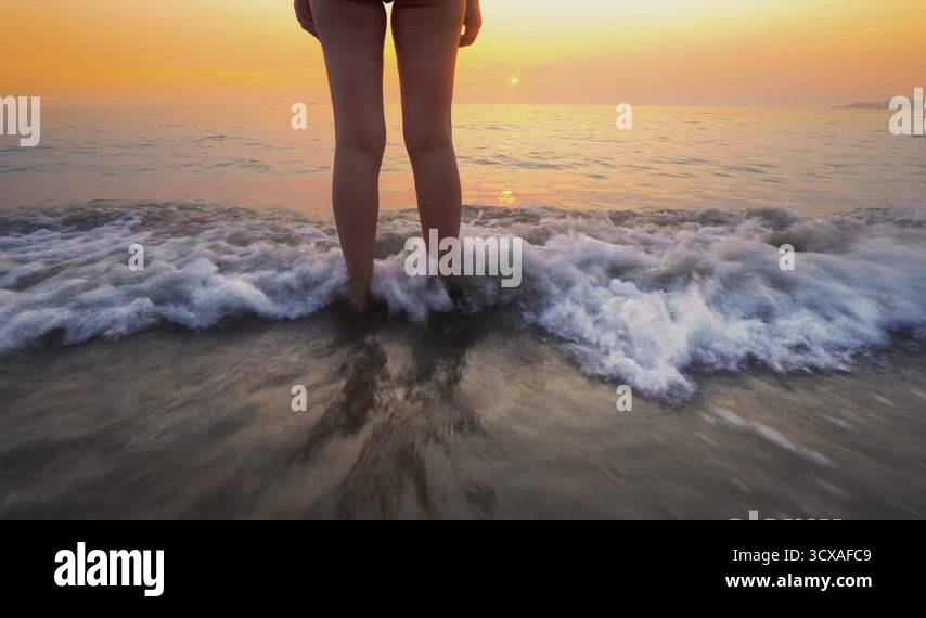 Woman feet splashed by sea waves on beach sunset. Calm serene relaxing ...
