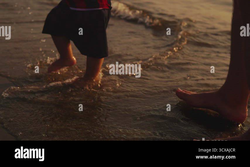 Close up of baby feet splashed by sea sunset waves on golden sand at ...