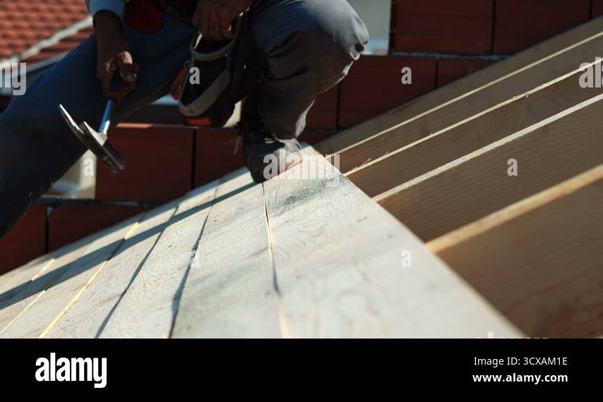 construction roofer carpenter worker nailing wood board with hammer on ...