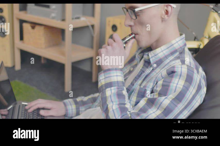 Exhaling smoke or vaping during working on laptop Young man relaxes ...
