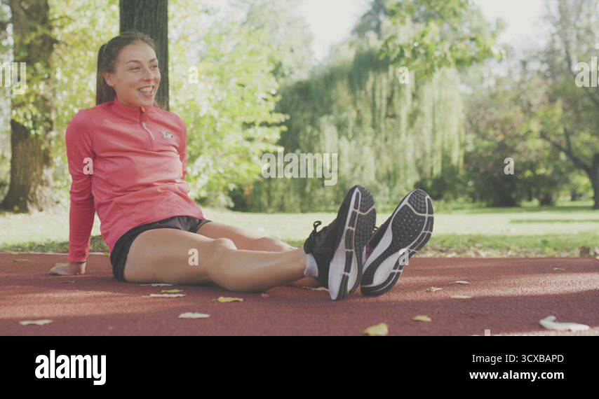 Fitness girl stretching her legs while sitting on an all weather ...