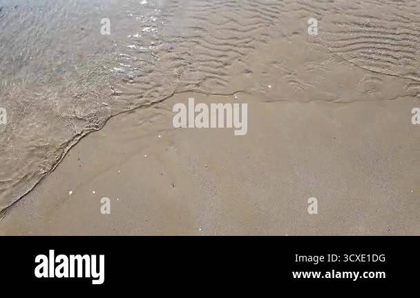 Close-up overhead view of very shallow, clear water retreating from the ...
