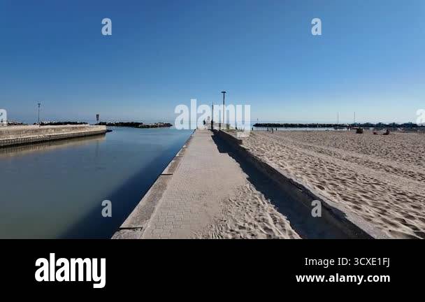 A concrete jetty separating a sandy beach from the calm, blue water of ...