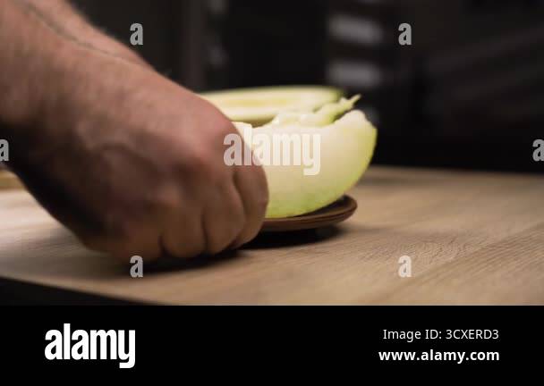 Man slicing fresh melon on pieces on wooden cutting board. yellow melon ...