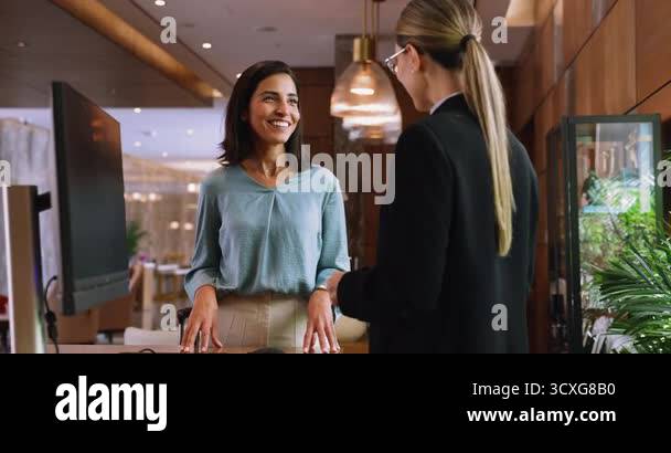 Friendly female hotel receptionist hands room keycard to woman guest at ...