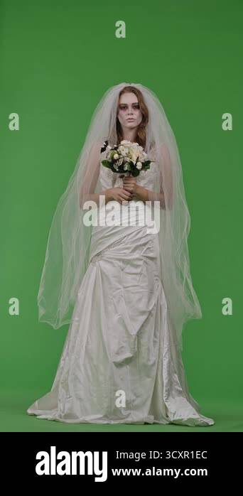 A woman dressed as a dead bride in a white wedding dress and veil holds ...