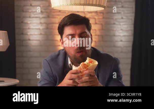 A businessman in a suit enjoys a delicious shawarma in a cozy cafe. An ...