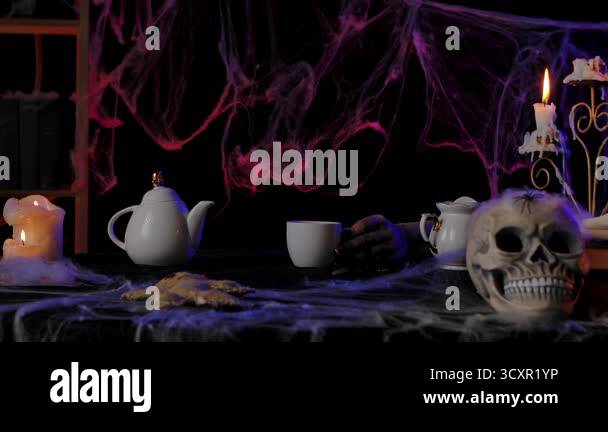 Scary zombie hands pour tea into a cup. A dark room with burning ...