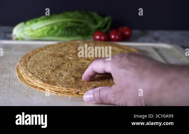 Hand is taking fresh tortillas layered on a cutting board alongside ...