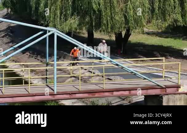 Workers repairing pedestrian bridge with tools, standing on concrete ...