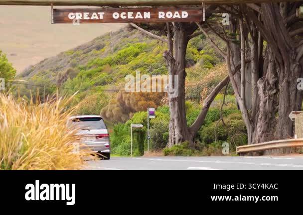 A car travels along the scenic Great Ocean Road, surrounded by lush ...