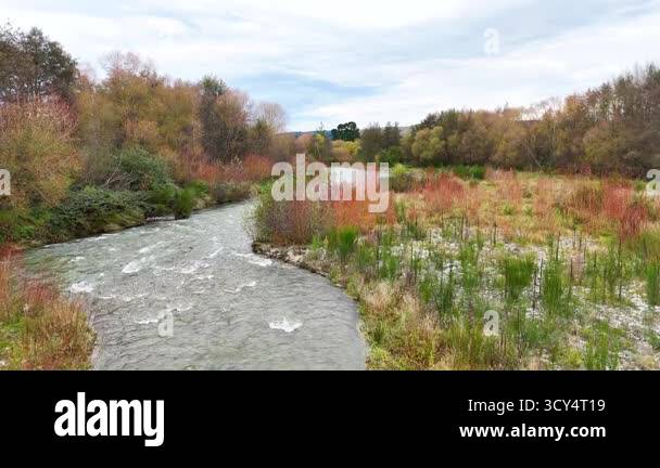 A tranquil river winds through vibrant autumn foliage under soft ...
