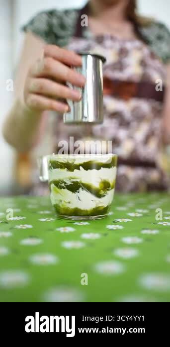 Chef sprinkling cocoa powder on a layered pistachio and cream dessert ...