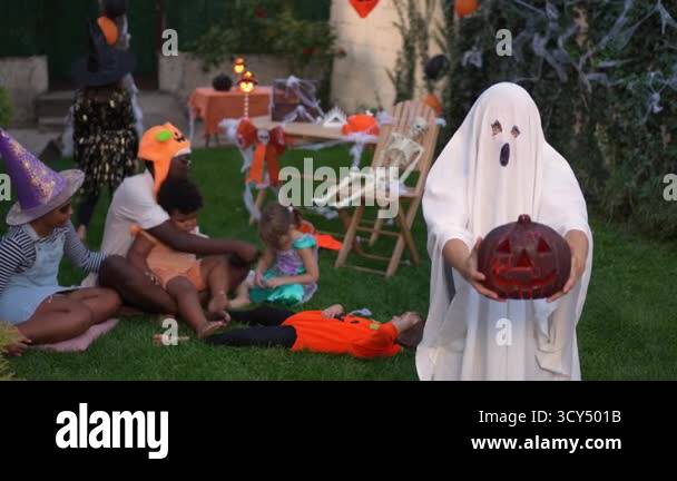Boy in a ghost costume holding a jack-o-lantern scaring a group of ...