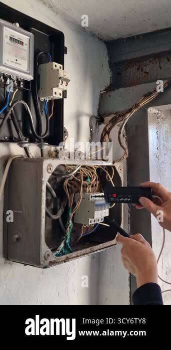 Hands of an electrician performing voltage test on exposed, messy ...