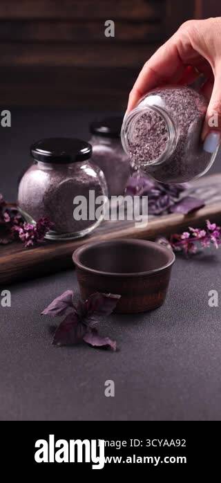 Purple basil salt being poured from a glass jar into a small clay bowl ...